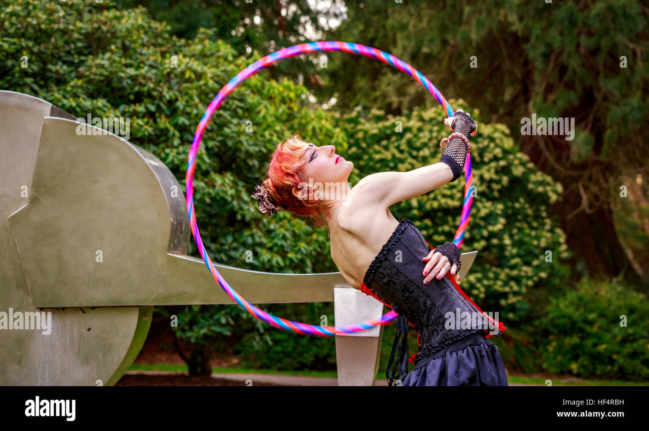 Young beautiful woman in circus costume play with hula hoop in the park ...
