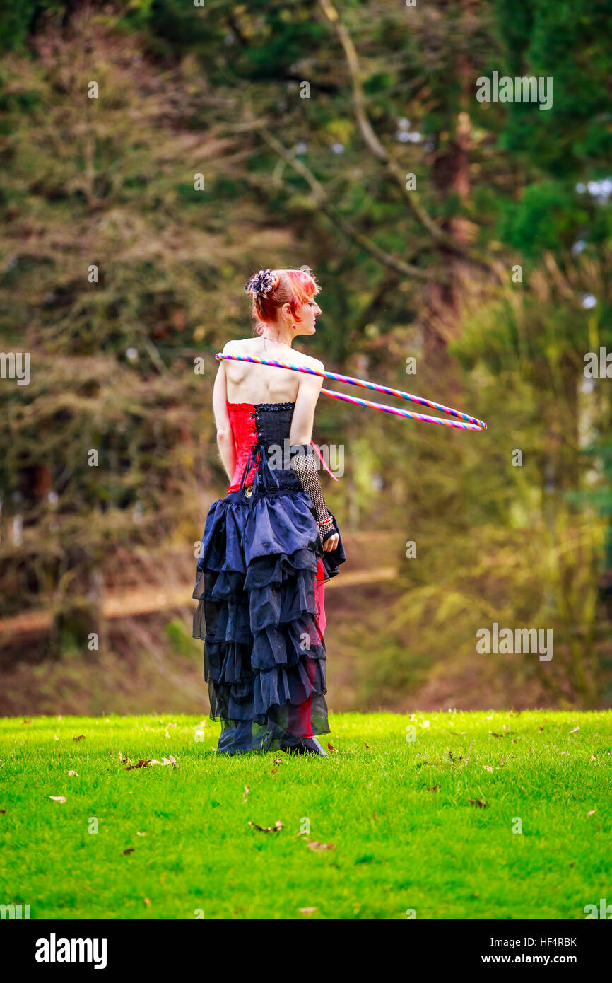 Young beautiful woman in circus costume play with hula hoop in the park ...