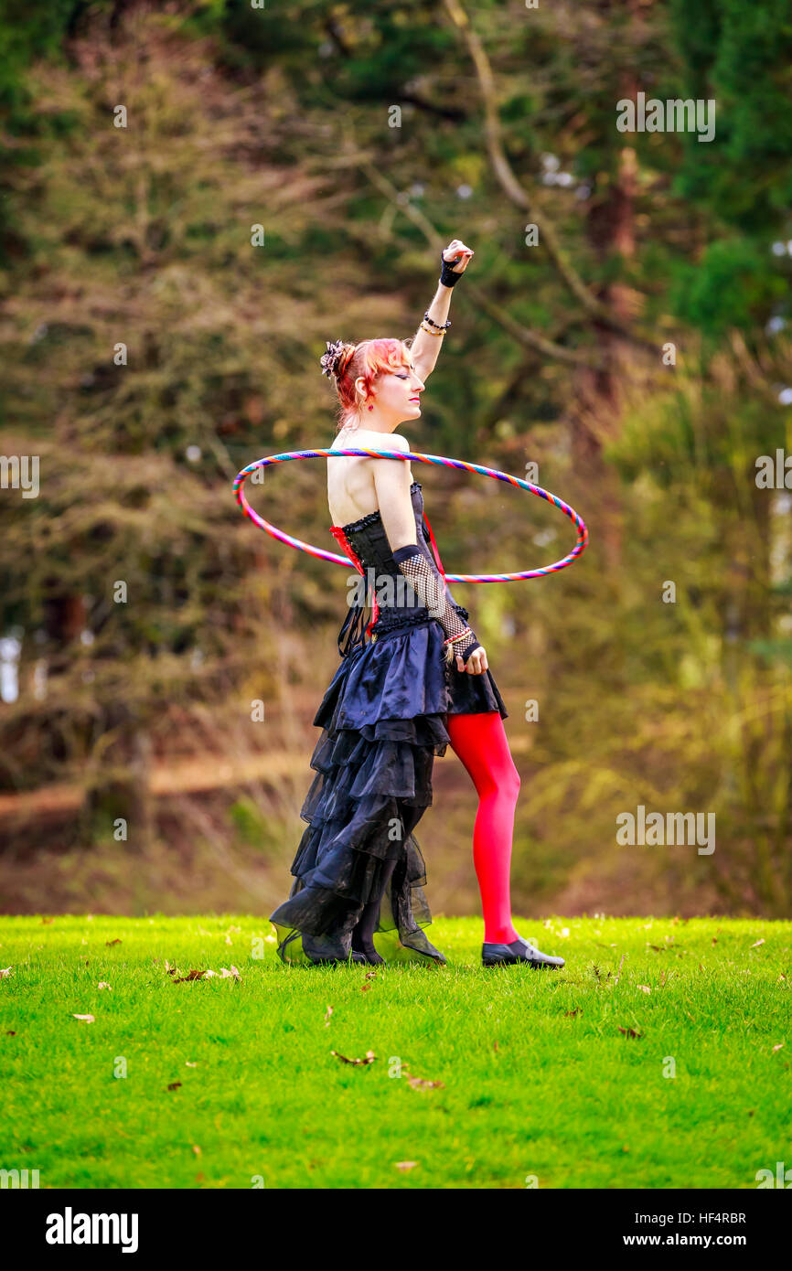 Young beautiful woman in circus costume play with hula hoop in the park ...