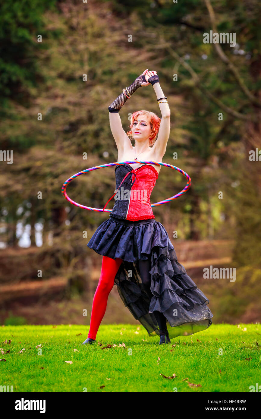 Young beautiful woman in circus costume play with hula hoop in the park ...