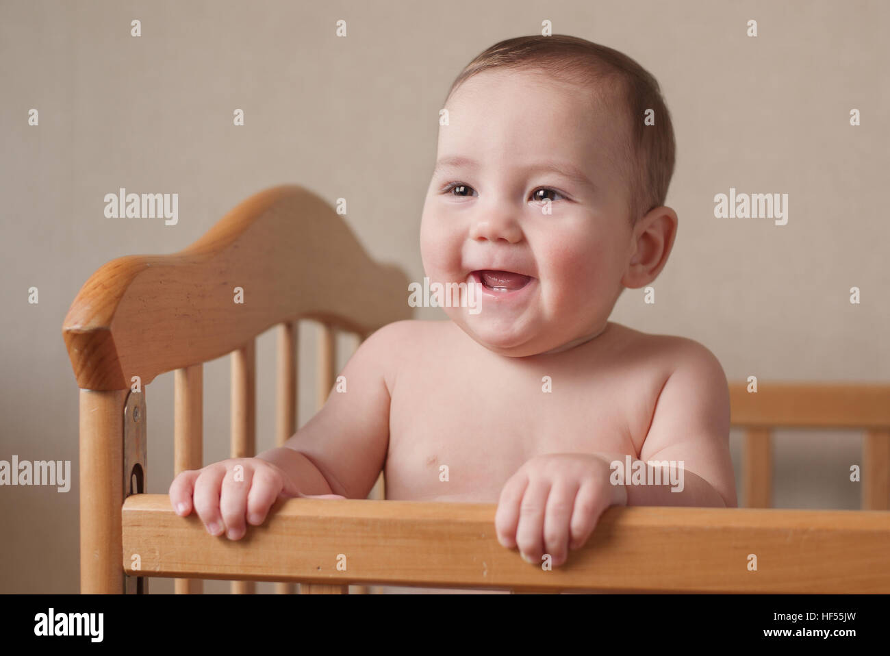 Adorable happy young baby with a lovely smile standing up in a wooden ...