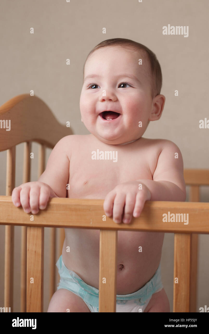 Adorable happy young baby with a lovely smile standing up in a wooden ...