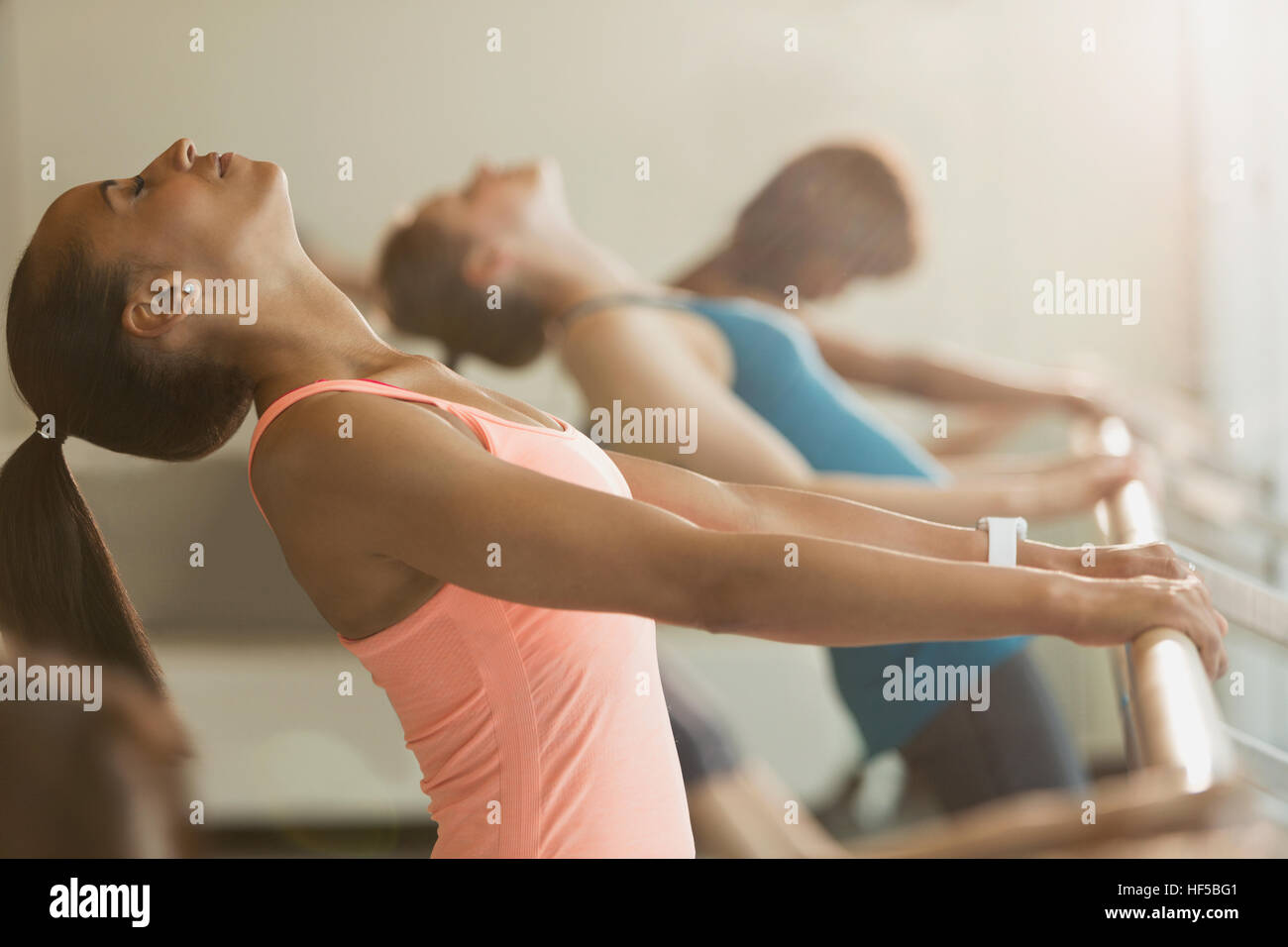 Women stretching in backbend at barre in exercise class gym studio ...