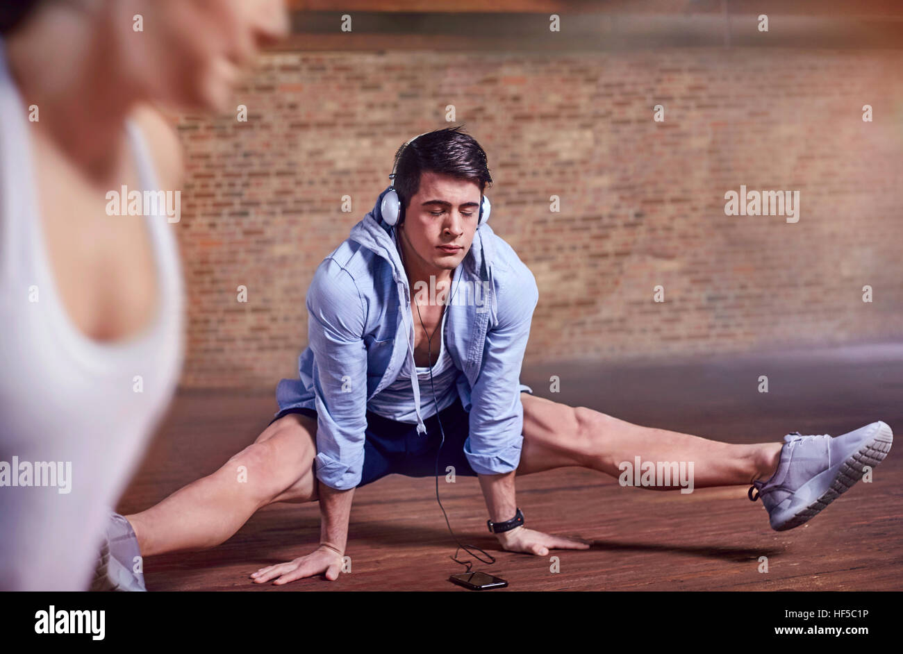 Focused young male dancer with headphones and mp3 player stretching in ...