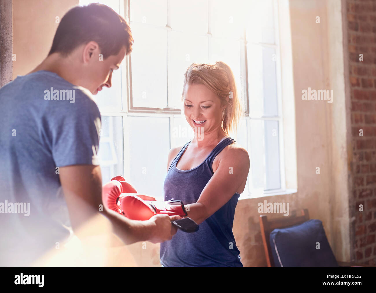 Trainer helping young female boxer putting on boxing gloves in studio ...