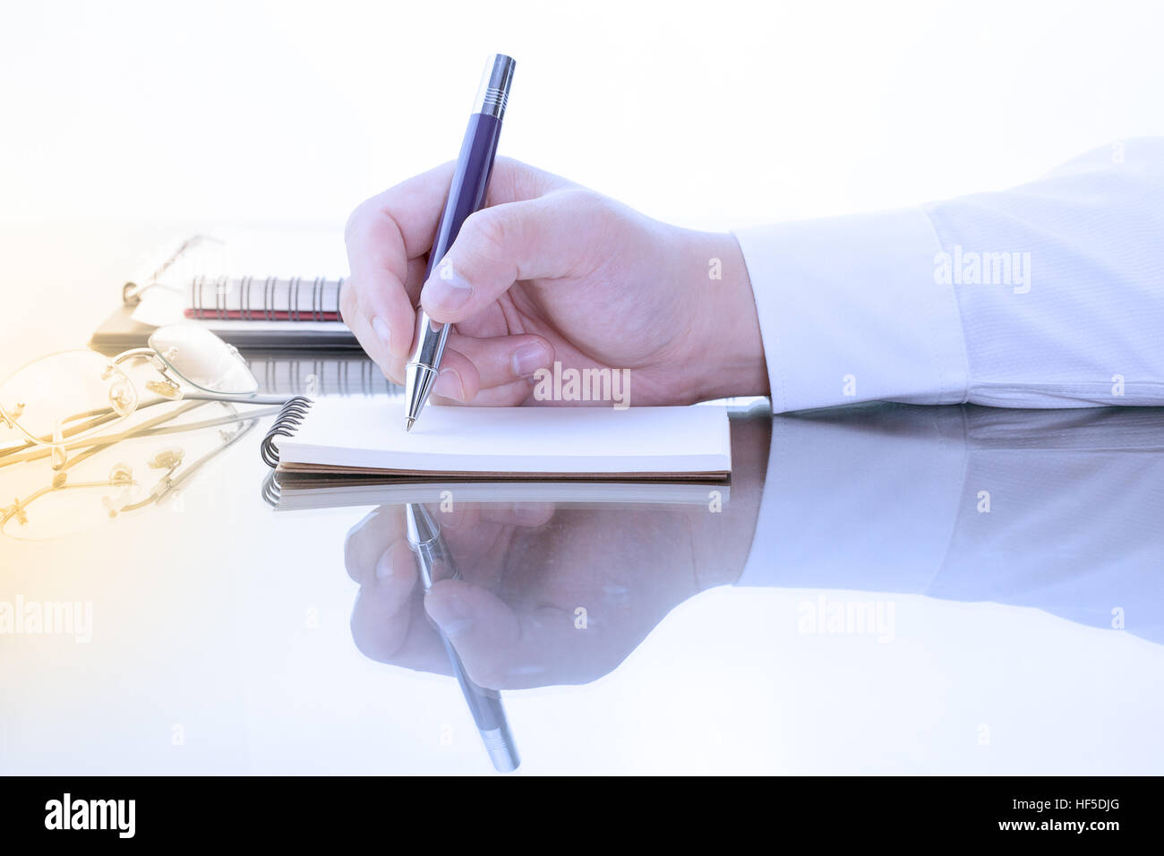 Businessman write a short note on opened notebook with pen and glasses ...