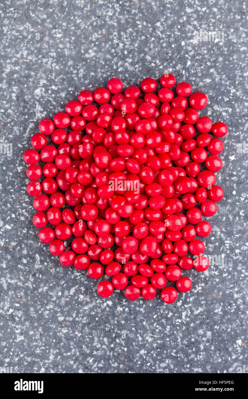 Red cinnamon candies on a mottled grey blue background Stock Photo - Alamy