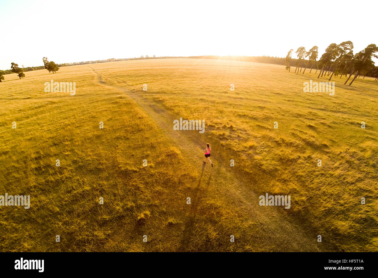 A female athlete is running into sundown across grassland Stock Photo ...