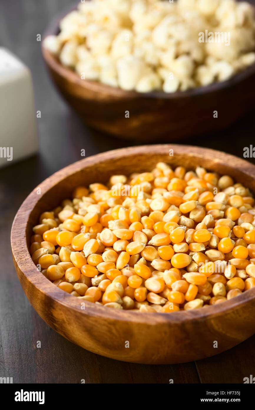 Yellow raw popcorn kernels in wooden bowl with salted popped popcorn in ...