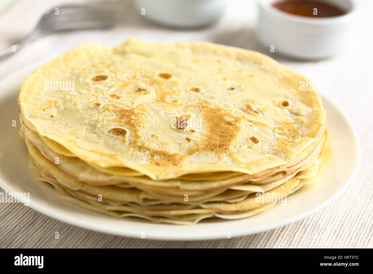 Freshly made crepes stacked on plate with jam in the back, photographed ...