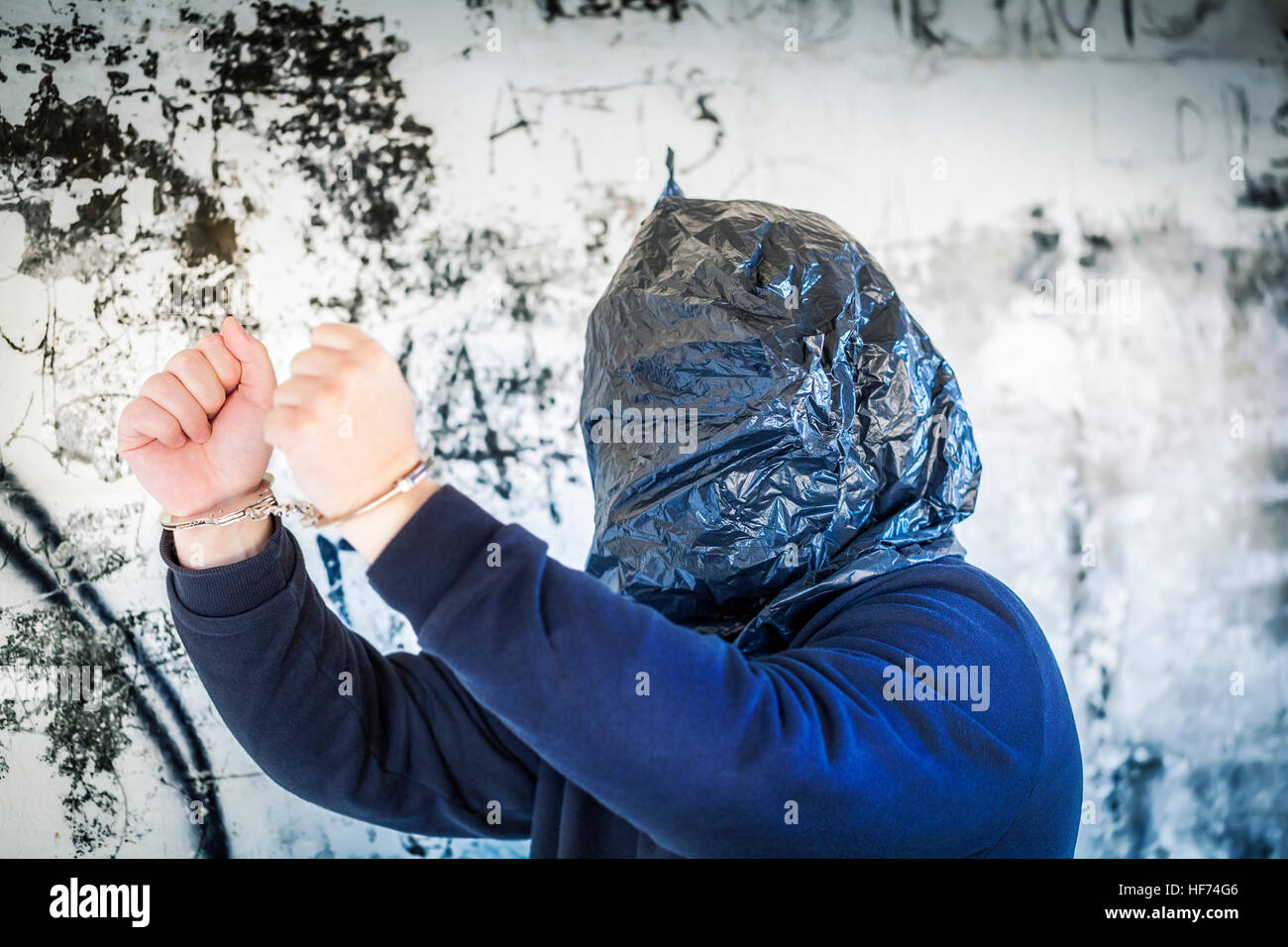 Hostage in handcuffs and with a bag on head near wall Stock Photo - Alamy