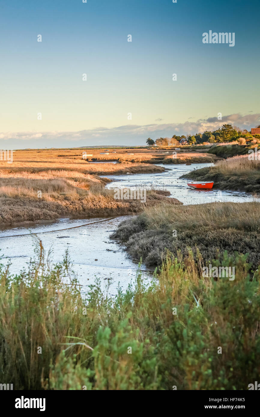 Salt marsh and estuary at low tide in Norfolk. A red dinghy is moored ...