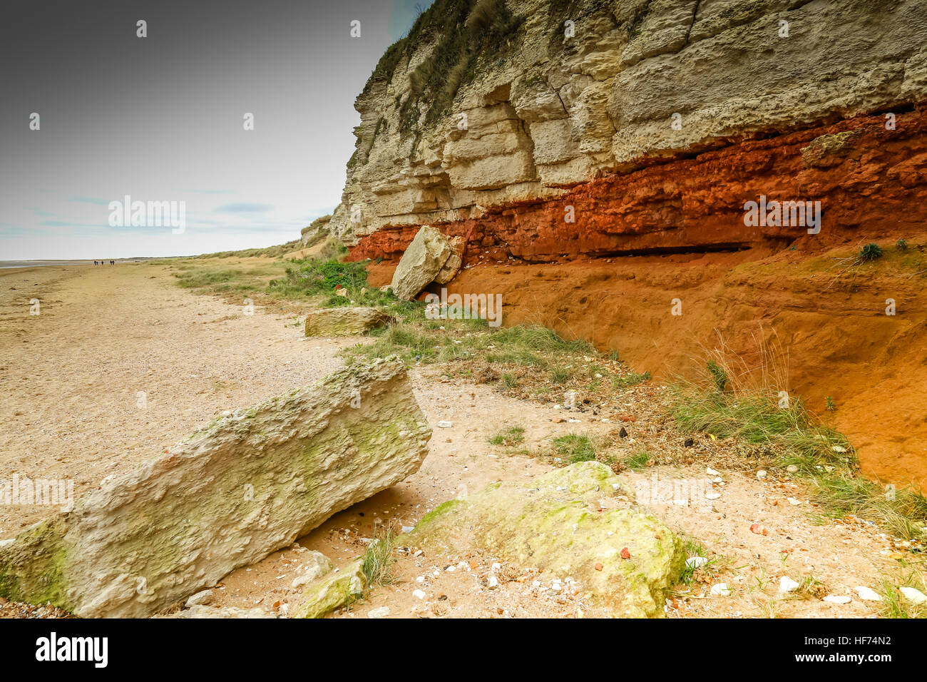 A large boulder at the foot of sea cliffs showing geological strata ...