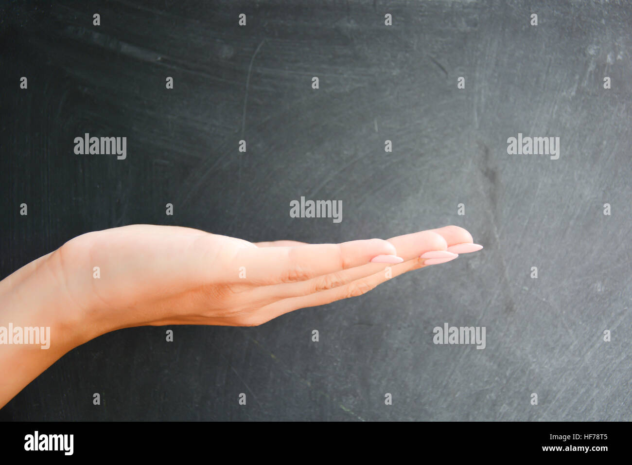 A woman's hand doing an explaining gesture in front of a blackboard ...