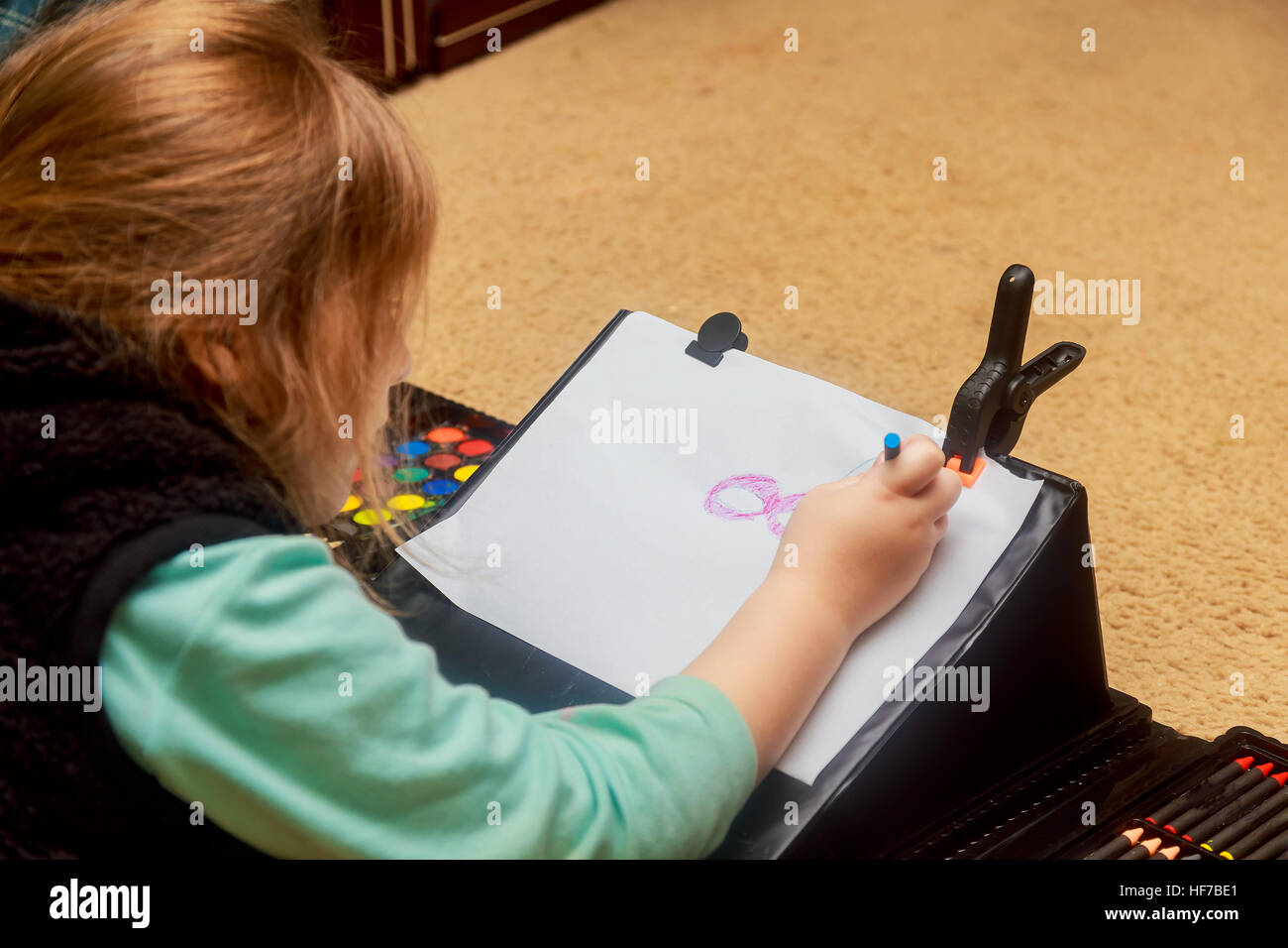Little girl is drawing using color pencils while laying on floor little ...