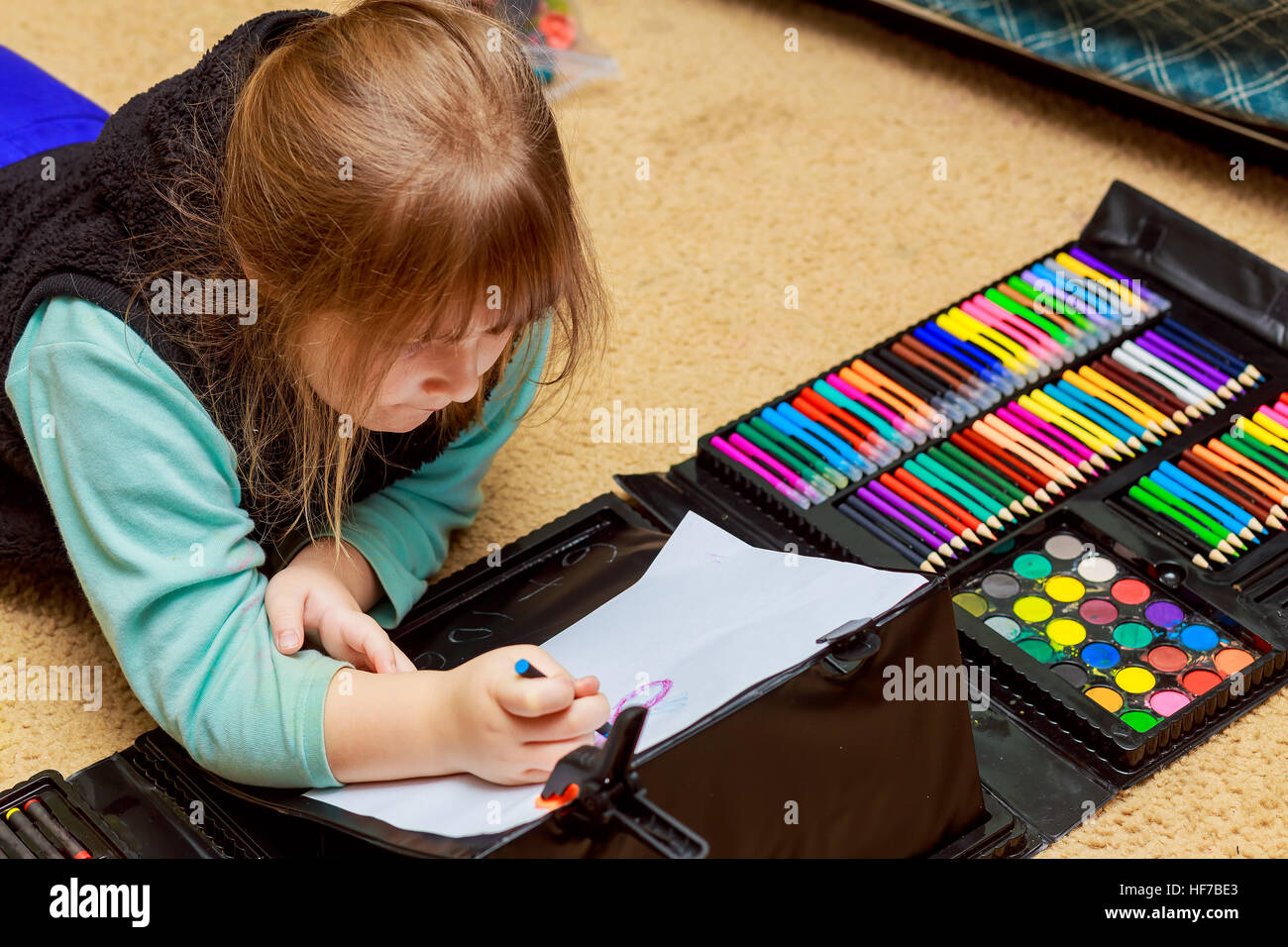 Little girl is drawing using color pencils while laying on floor little ...