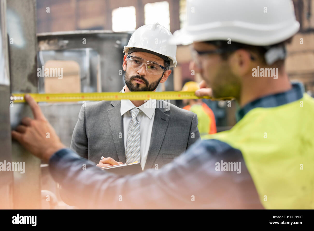 Manager watching steel worker with tape measure in factory Stock Photo ...