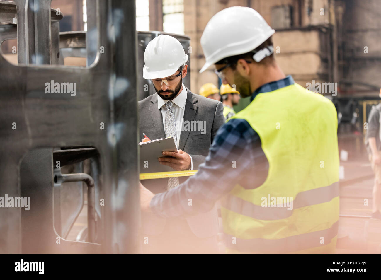 Manager with clipboard and steel worker with tape measure in factory ...