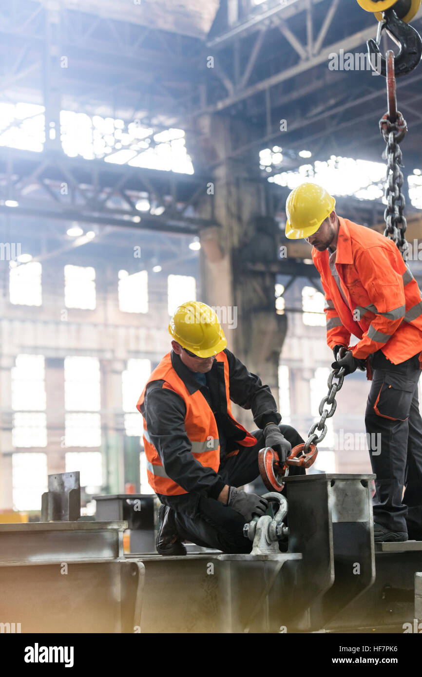 Steel workers fastening crane chain to steel in factory Stock Photo - Alamy