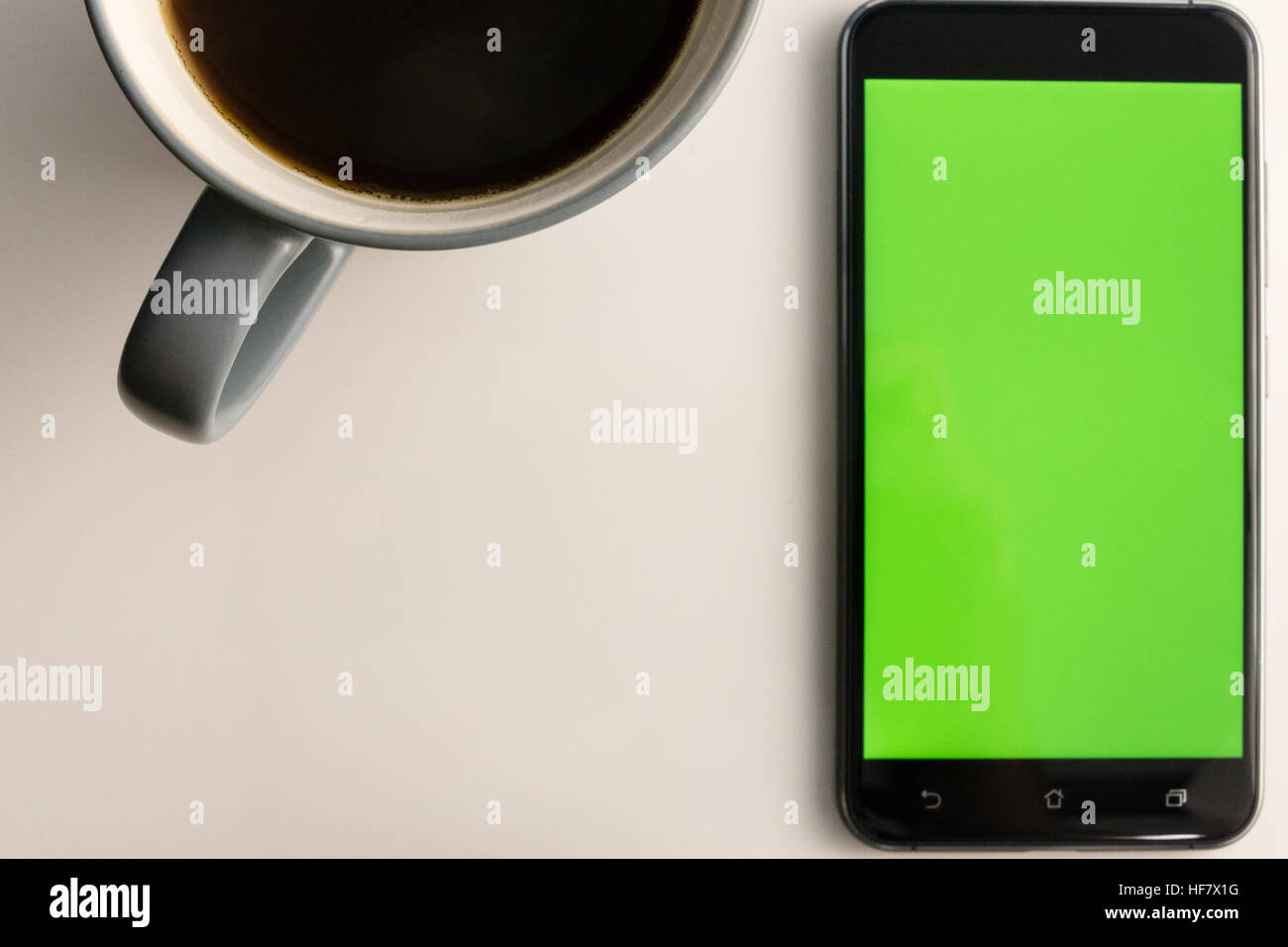 Smart phone with green screen on display next to coffee cup Stock Photo ...