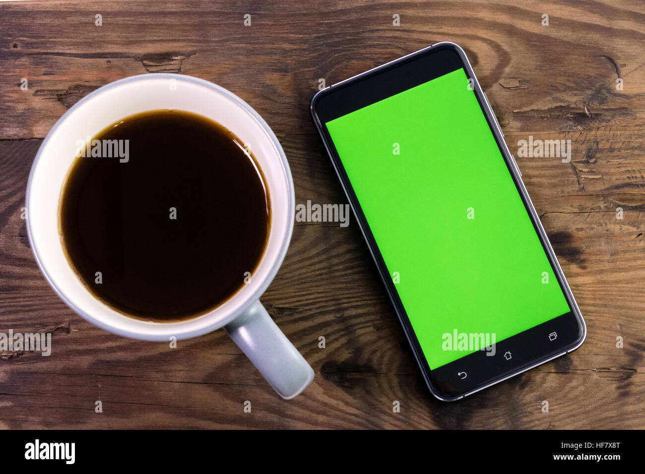Smart phone with green screen on display next to coffee cup, distressed ...