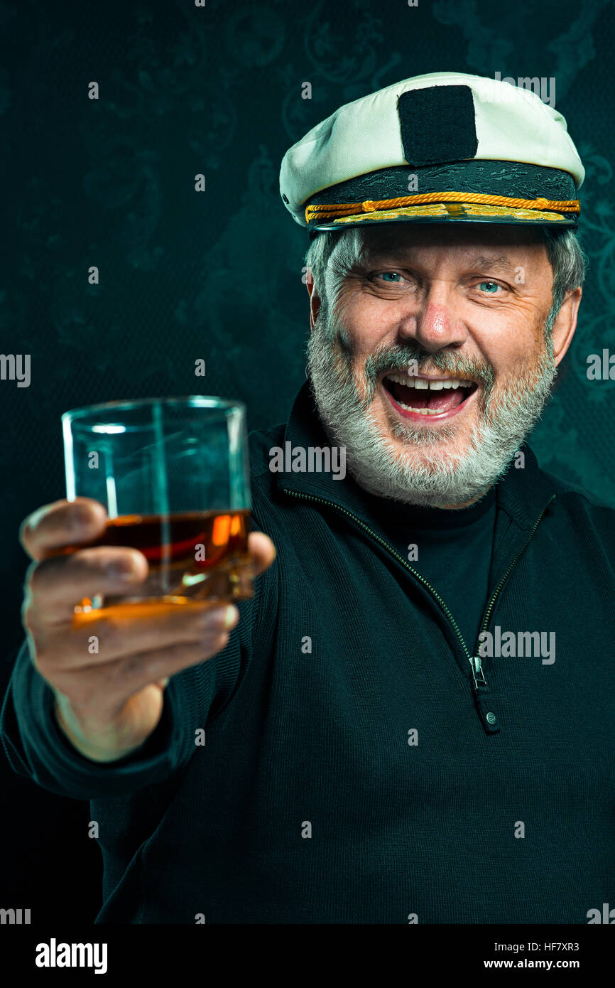 Portrait of old sailor man as captain in black sweater and hat drinking ...