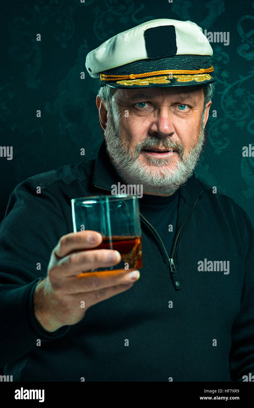 Portrait of old sailor man as captain in black sweater and hat drinking ...