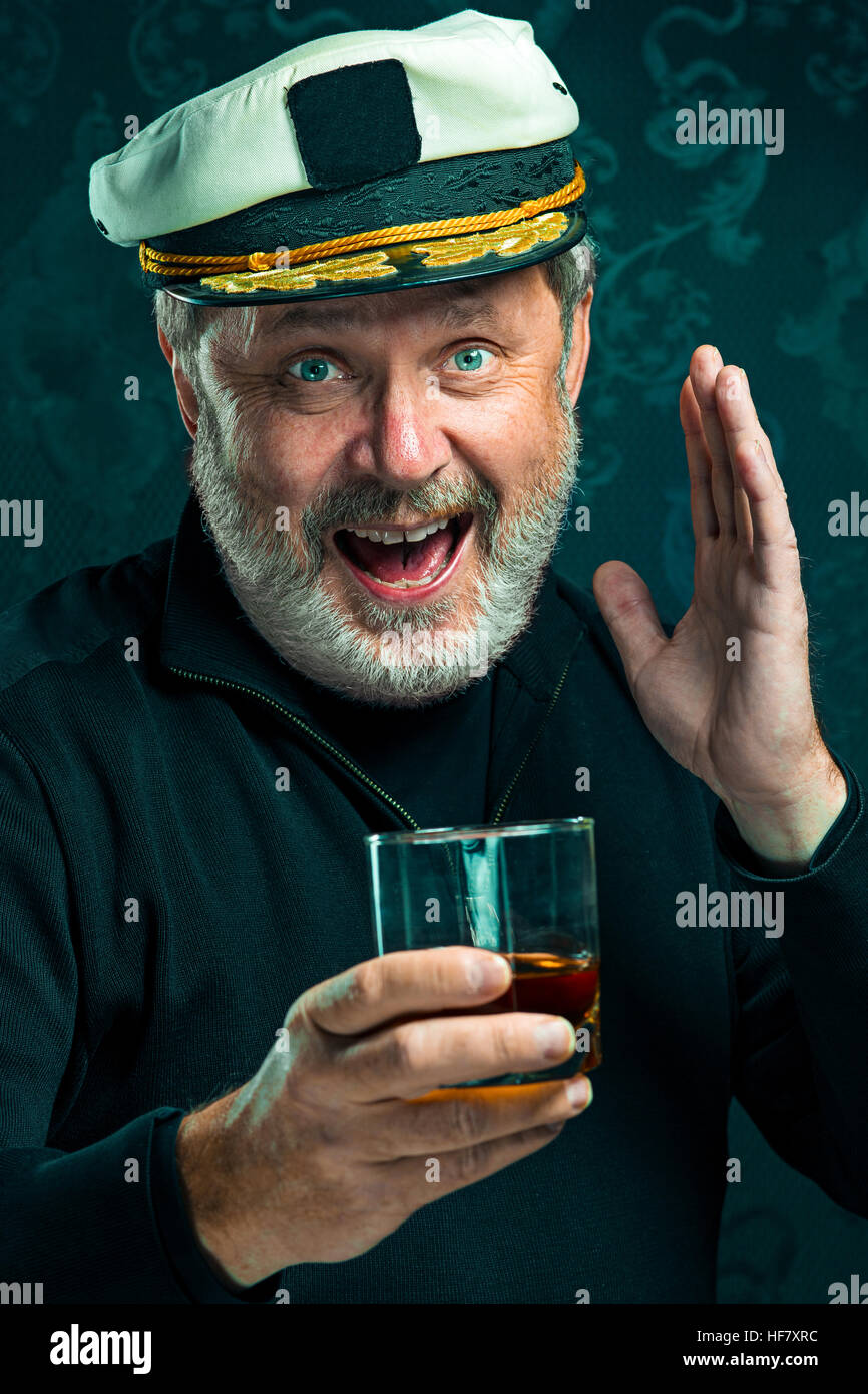 Portrait of old sailor man as captain in black sweater and hat drinking ...