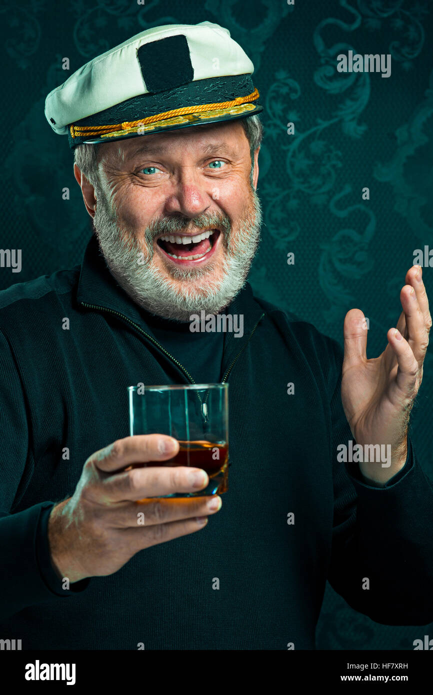 Portrait of old sailor man as captain in black sweater and hat drinking ...