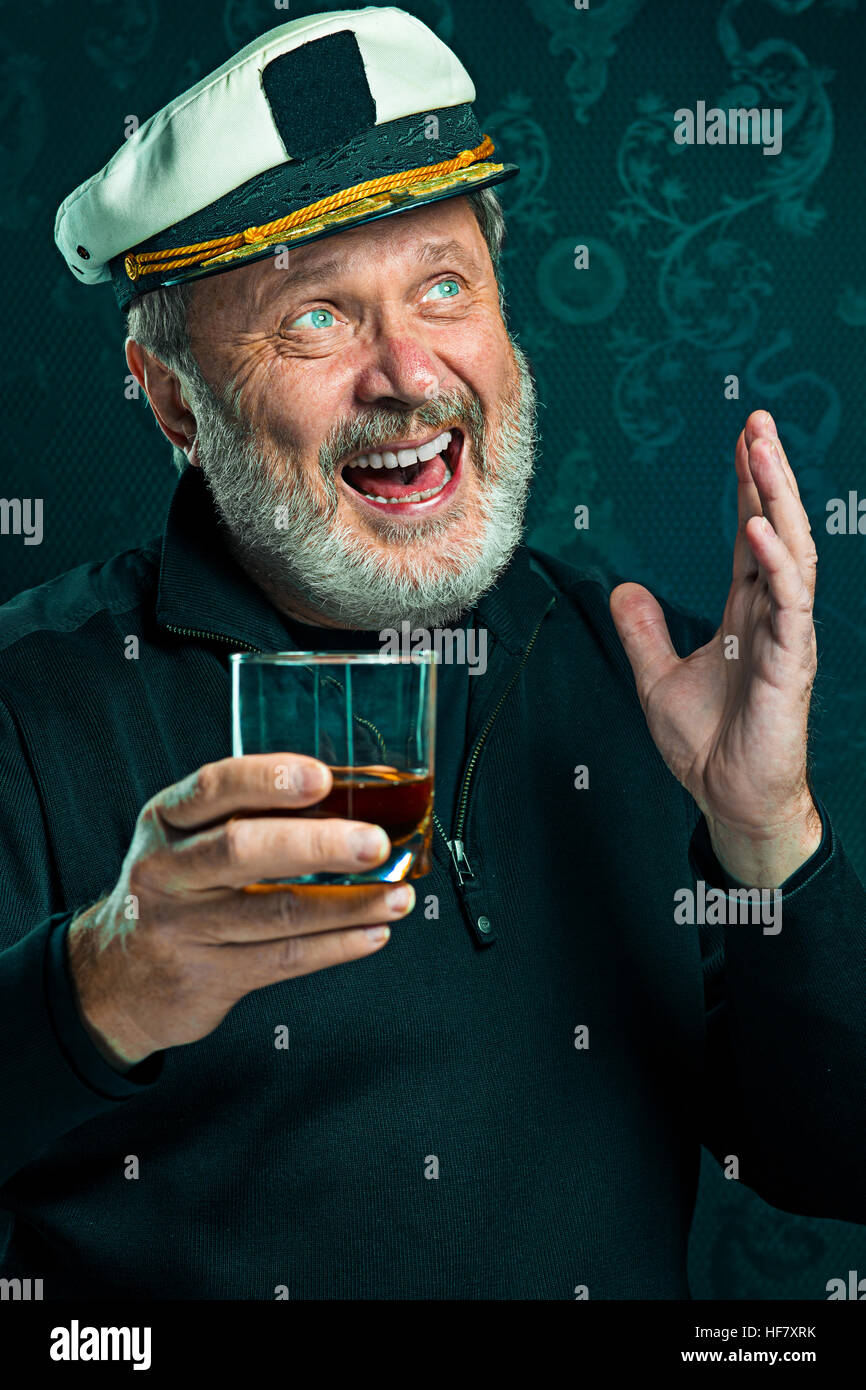 Portrait of old sailor man as captain in black sweater and hat drinking ...