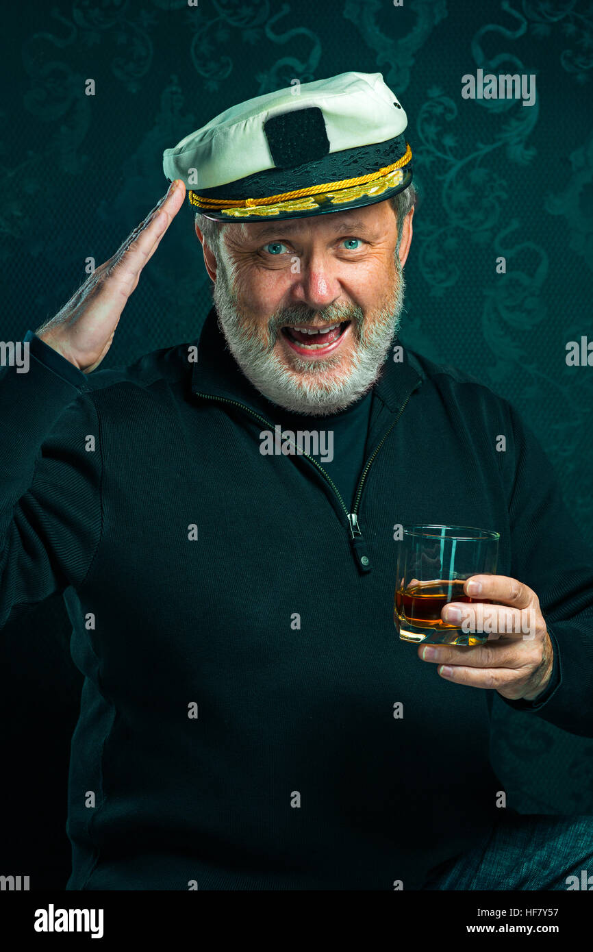 Portrait of old sailor man as captain in black sweater and hat drinking ...