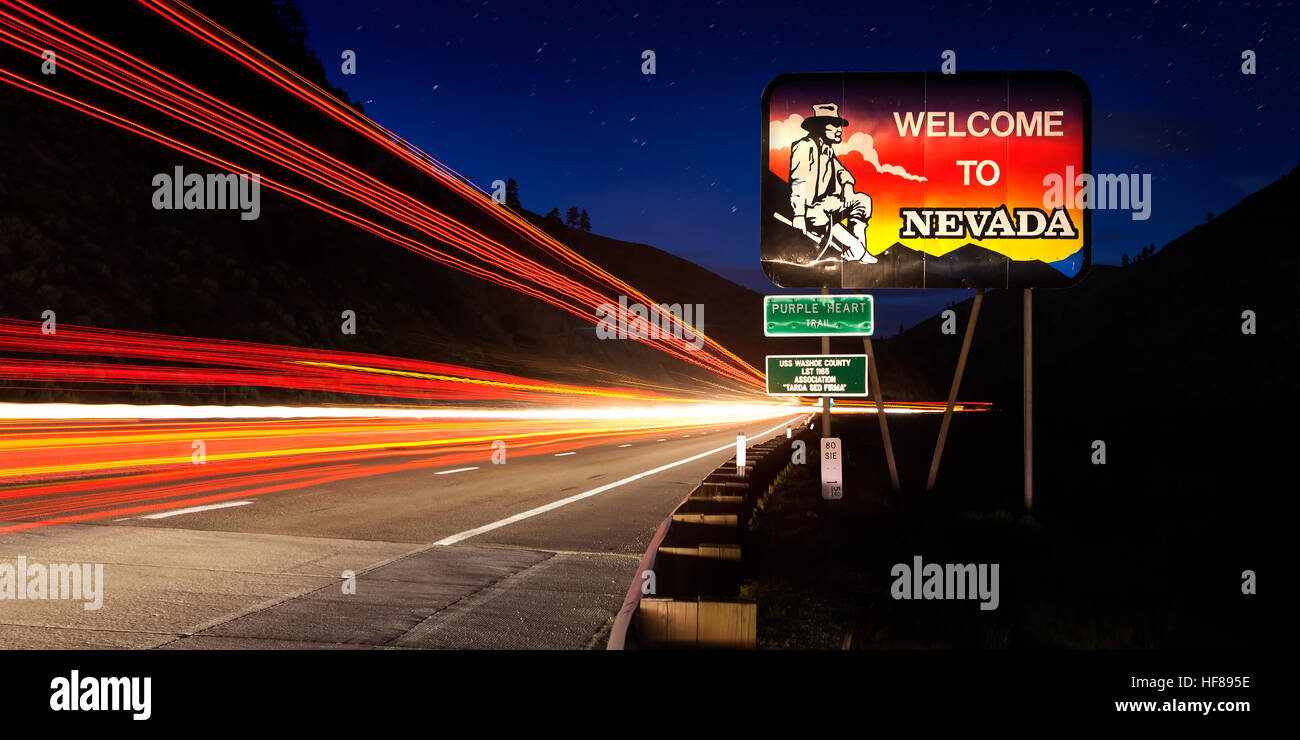 Nevada State line road sign with long exposure traffic trails at night ...