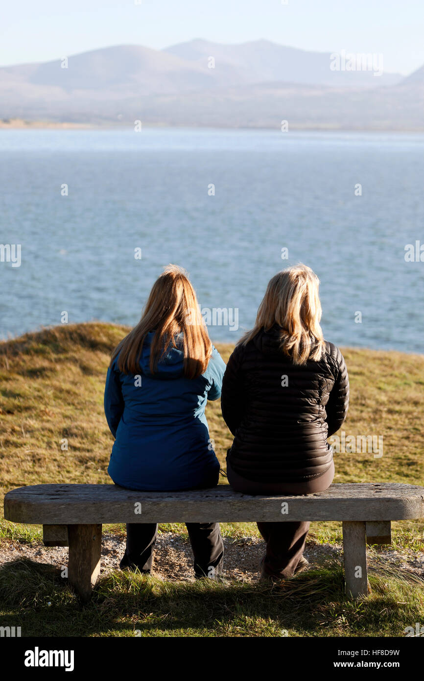 Two female friends sitting side by side with backs turned on a bench ...