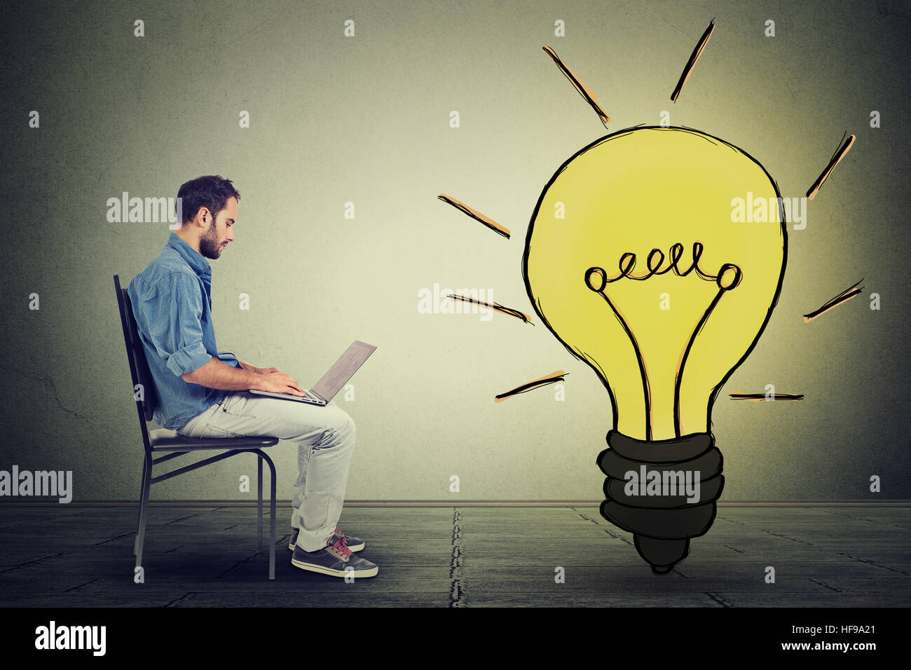 Side profile young man using laptop with light bulb on gray wall ...