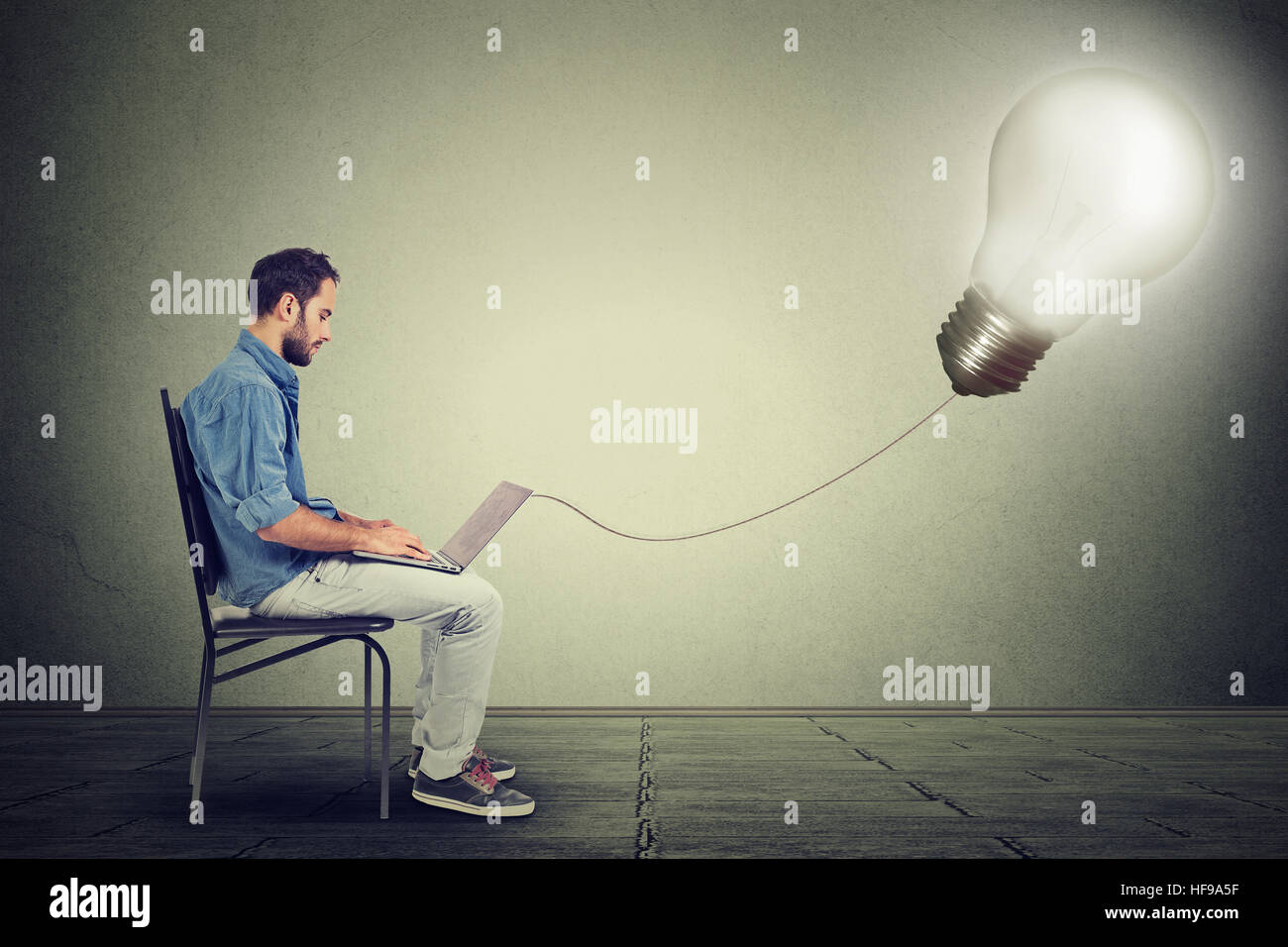 Young professional man using a laptop with light bulb plugged in it ...