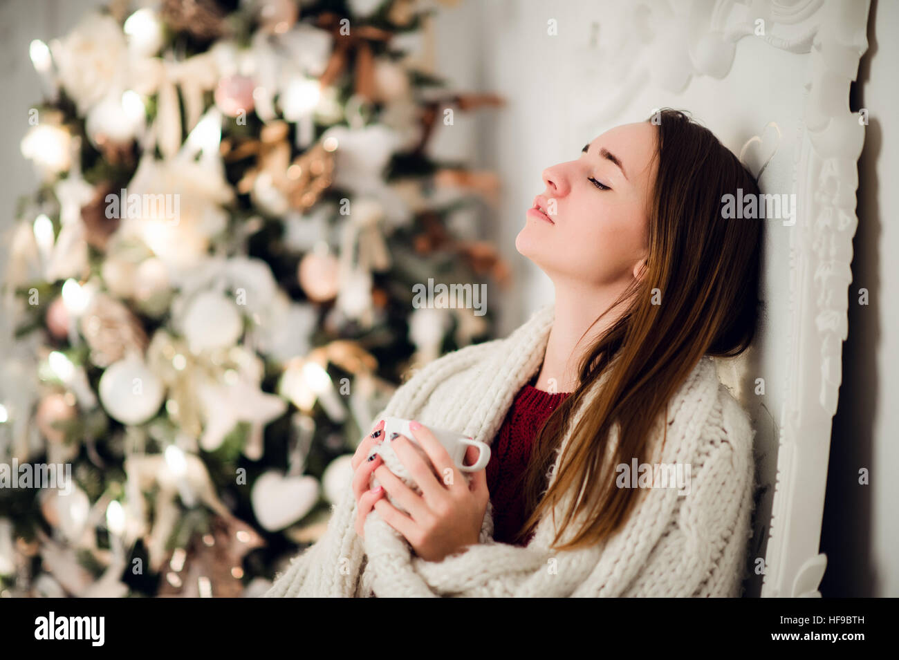 Young woman relaxing with a mug of coffee as she cuddles up in warm ...
