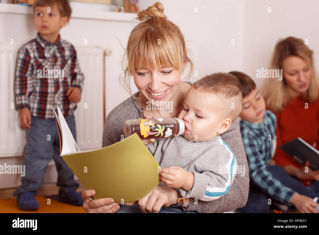 Young smiling woman reading a book to a toddler while another woman ...