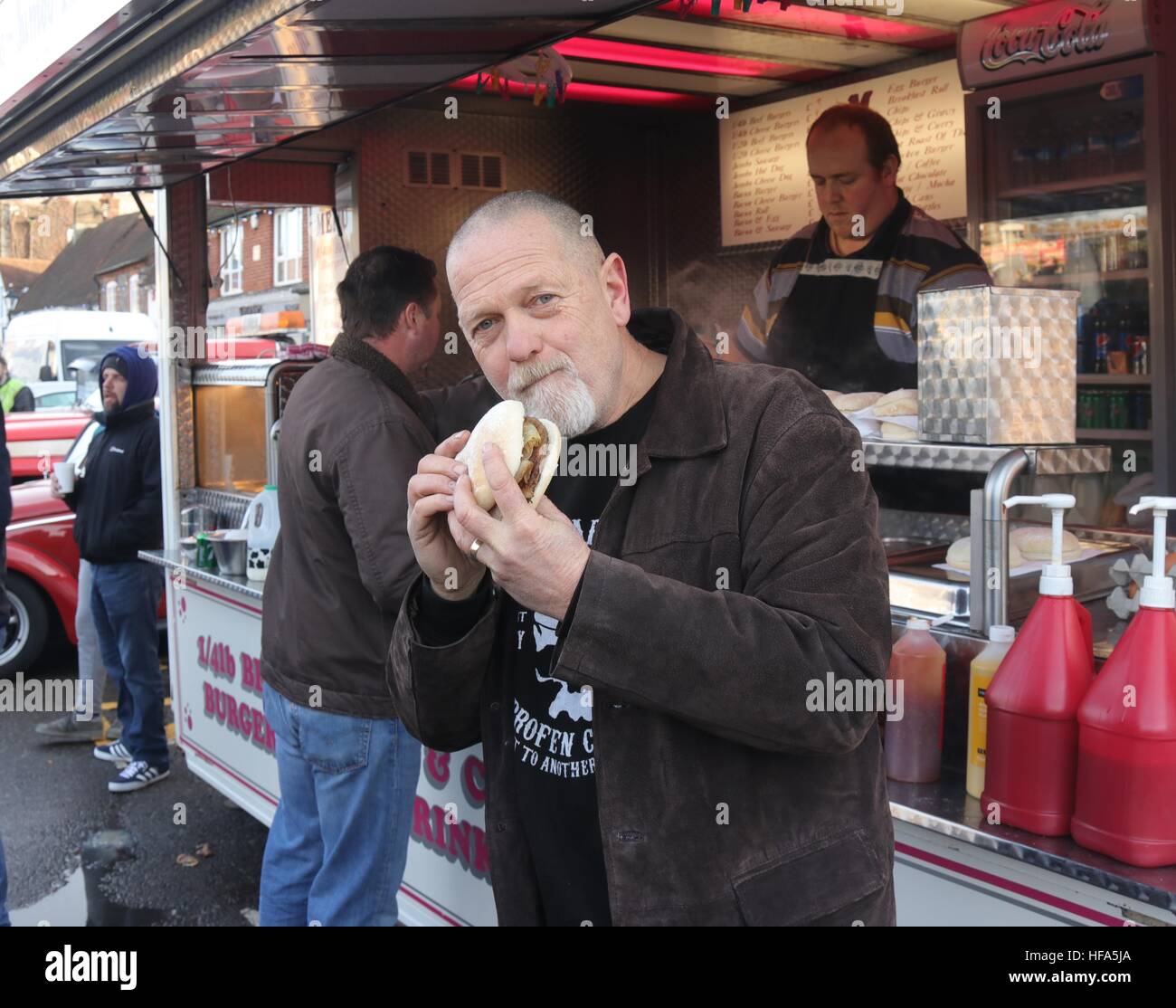 A handsome man eating a beef burger from a burger van Stock Photo - Alamy