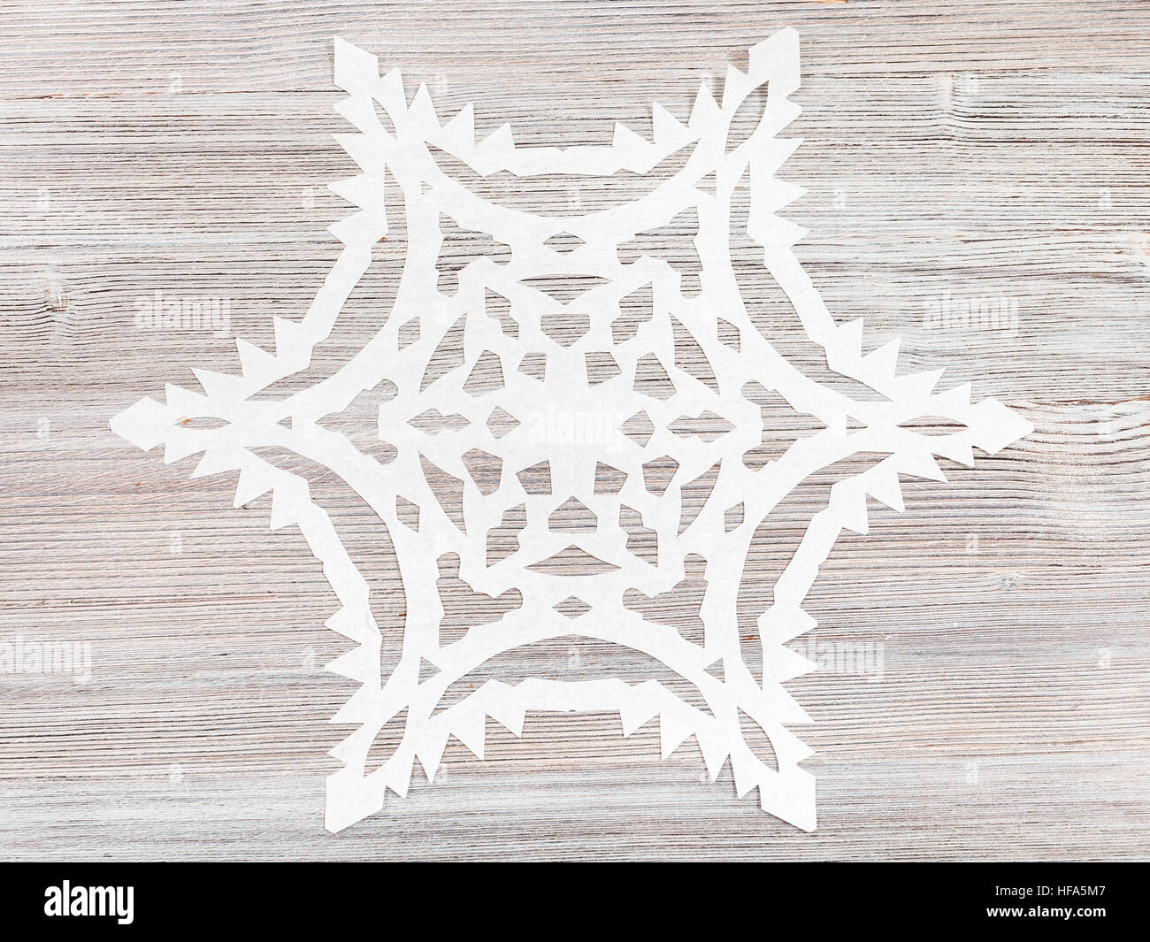 top view of snowflake carved from paper on light brown wooden surface ...