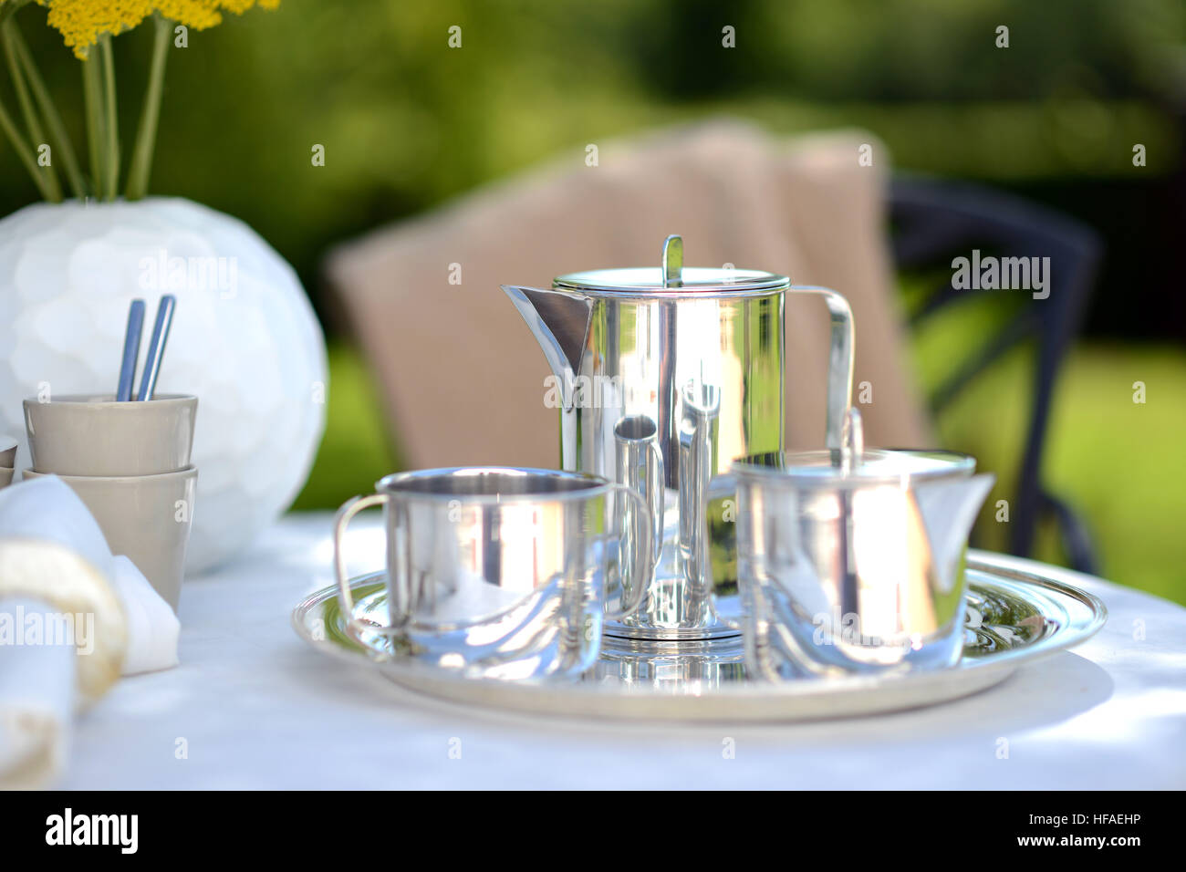 Luxury silver coffee pot on a linen covered table outside in summer ...