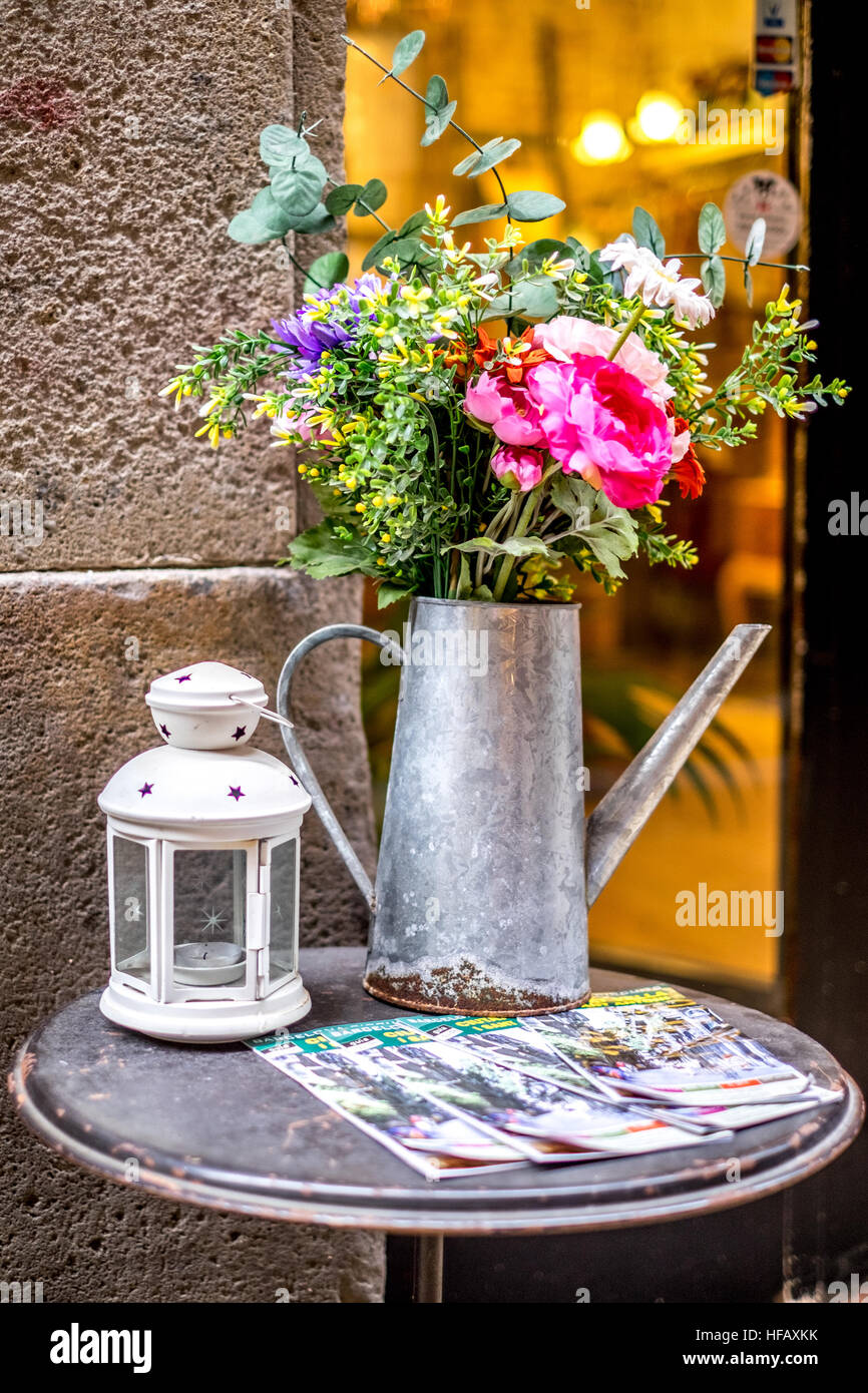 A beautiful colorful watering can full of flowers sits on street side ...