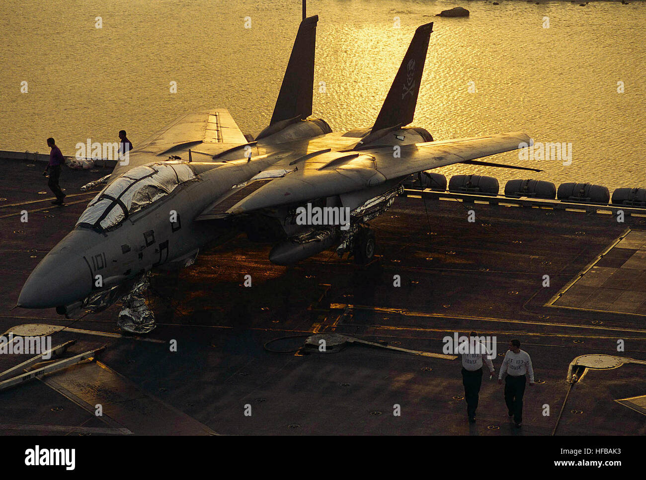 The rising sun glimmers on the water behind an F/14 Tomcat, from Fighter Attack Squadron One ...