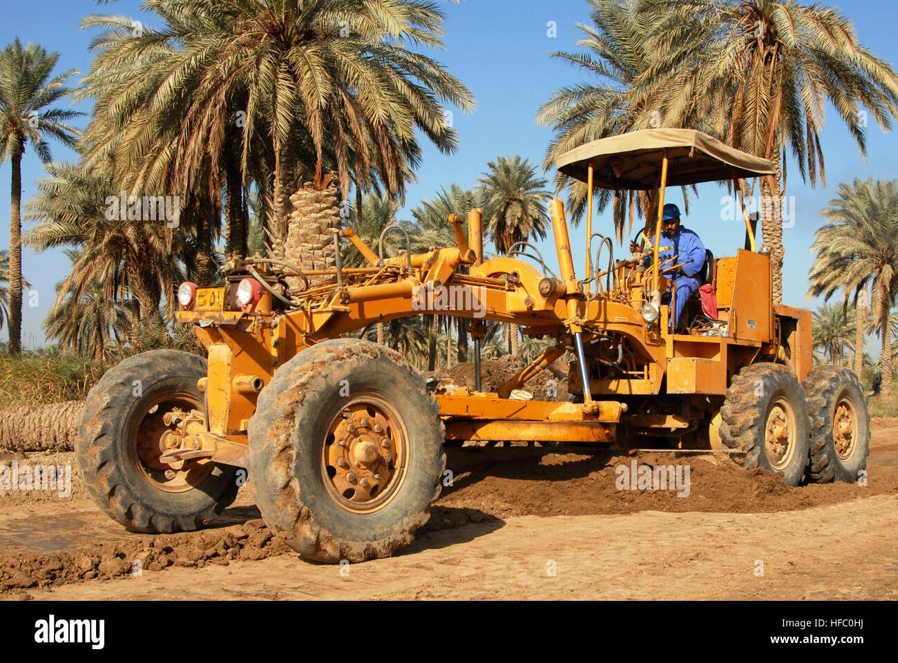 An Iraqi worker uses a grader equipment to grade the soil prior to ...
