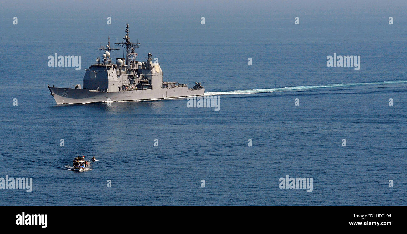 Guided-missile cruiser USS Chosin (CG 65) maneuvers past a fishing dhow ...