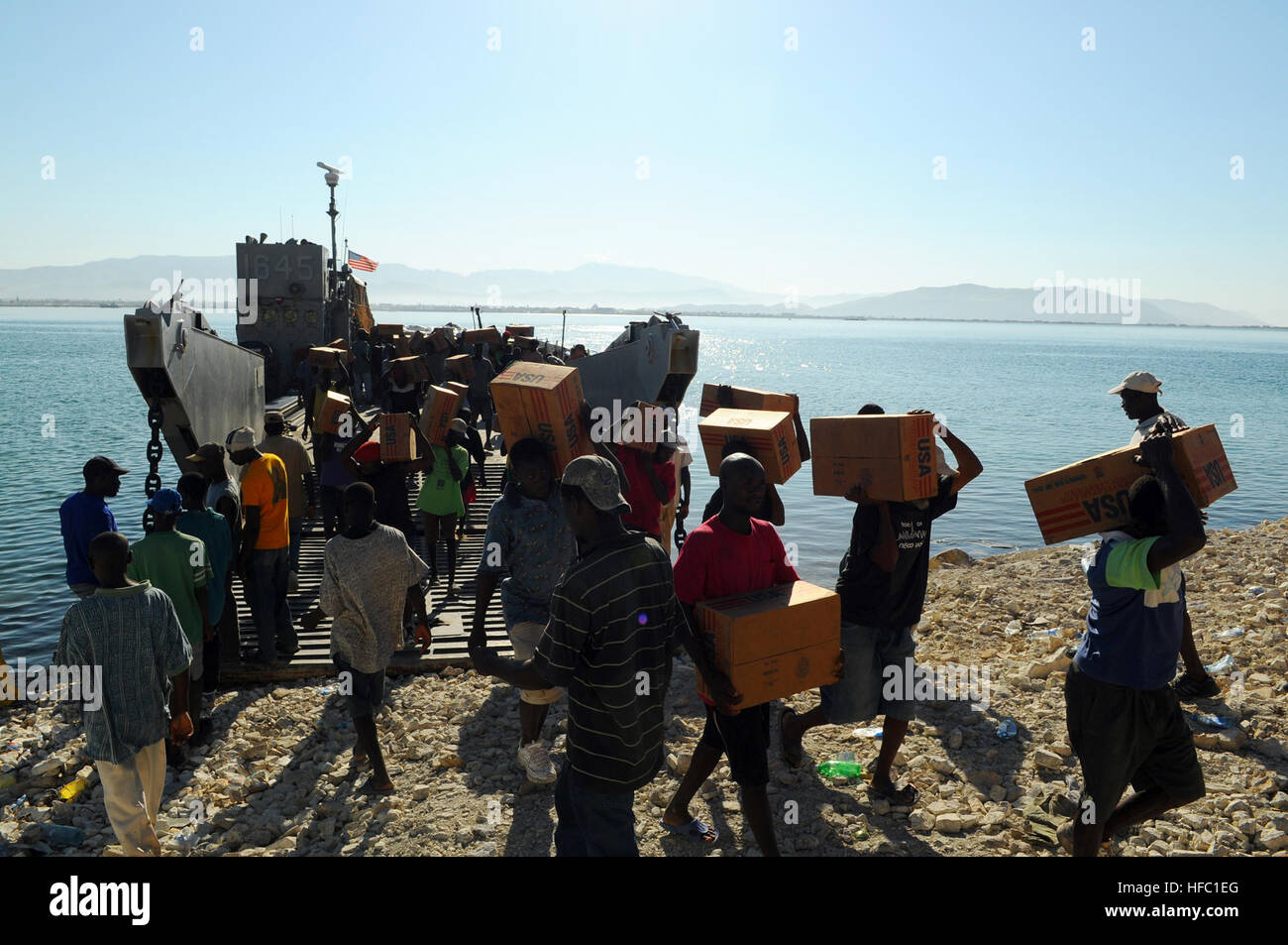 Haitian civilians unload humanitarian relief supplies from a landing ...