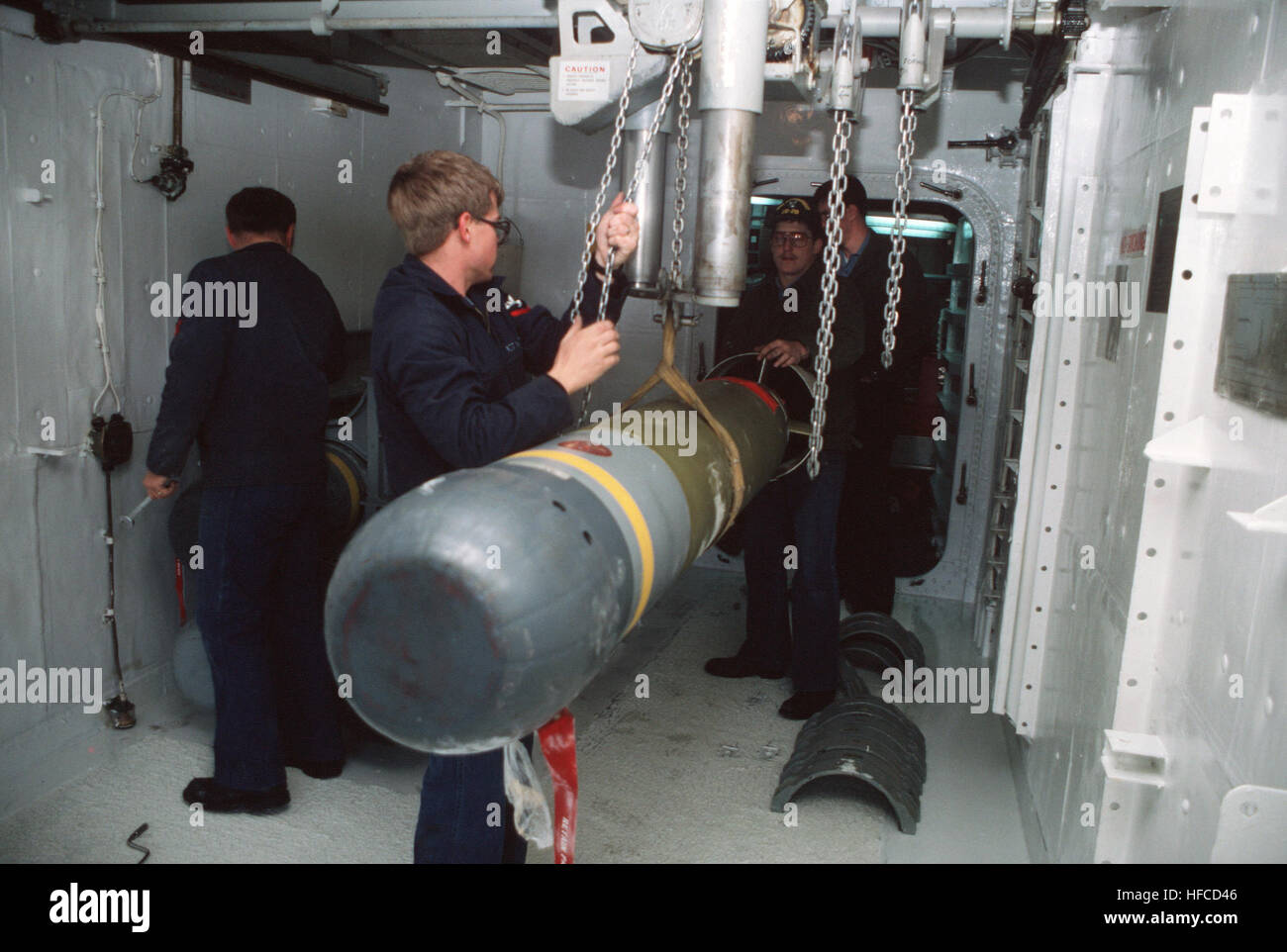 Crew members hoist a Mark 46 torpedo onto a storage rack during a ...