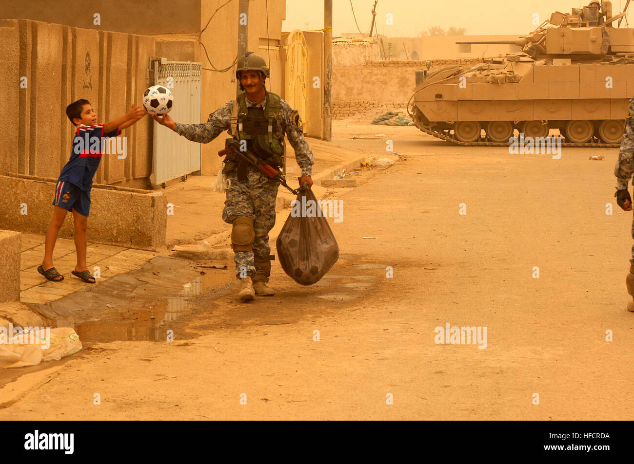 An Iraqi boy reaches out to receive a soccer ball from a policeman ...