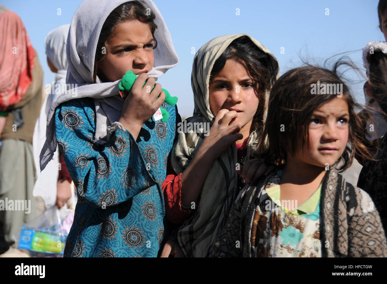 Three Farahi girls stand amongst a crowd waiting to receive assistance ...