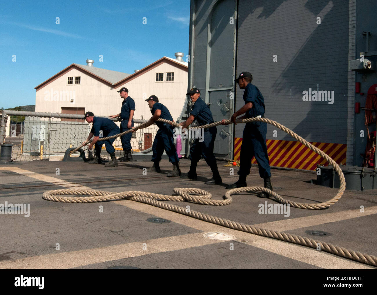 U.S. sailors handle a mooring line on the flight deck of guided missile ...