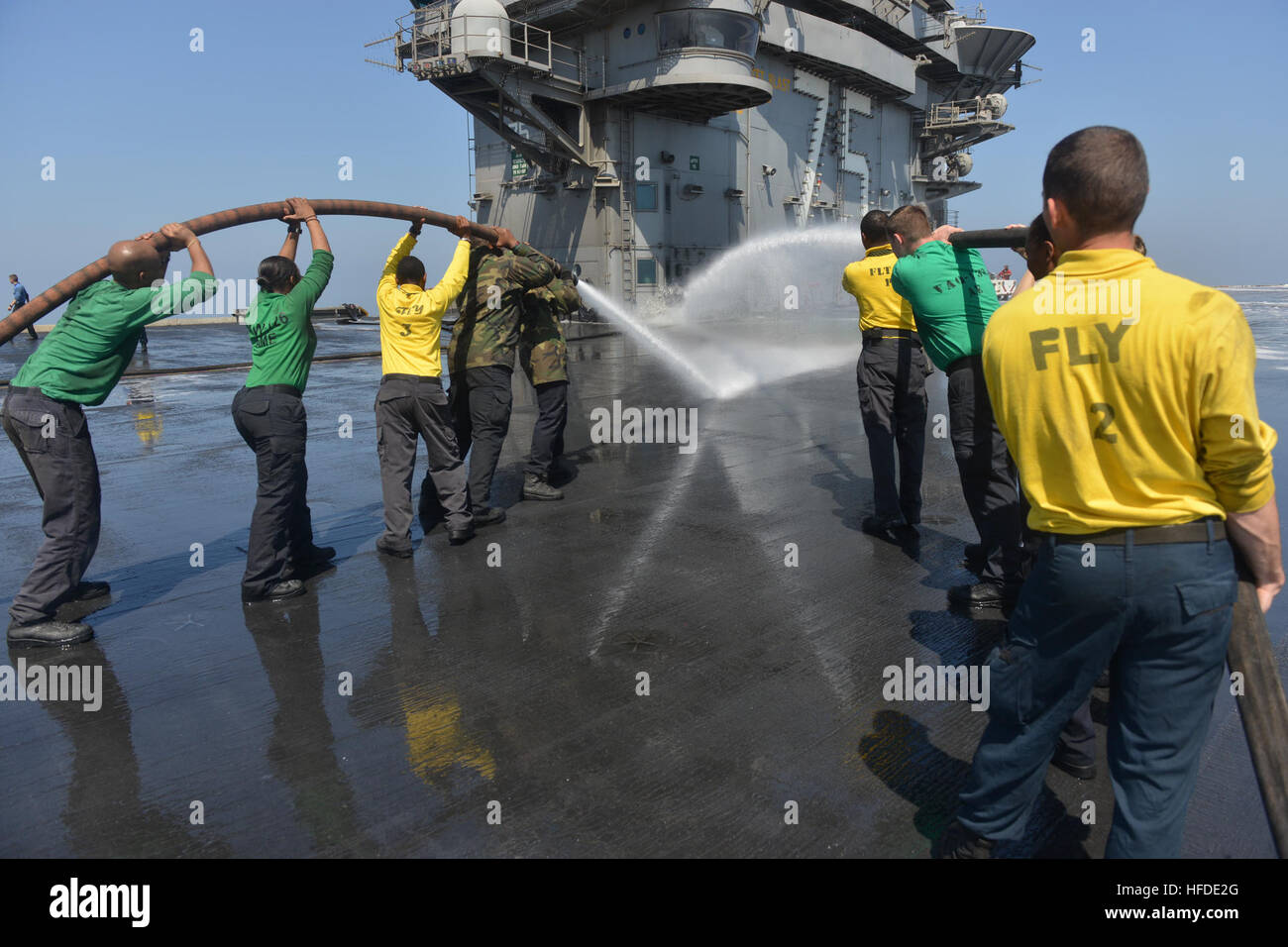 U.S. Sailors use fire hoses to wash down the flight deck of the ...